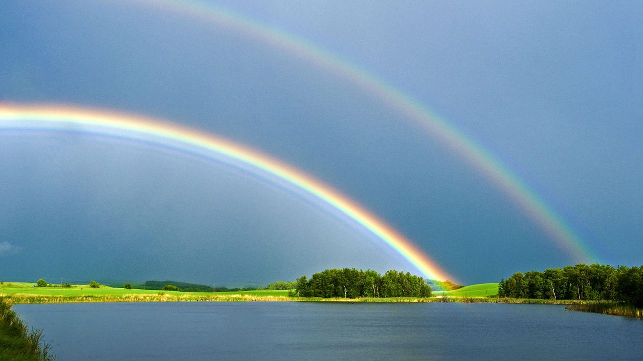 Prairie slough with farmland and rainbow in the background, near ...